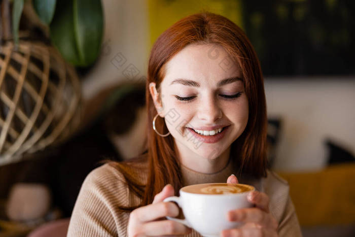 年轻快乐的女人微笑着拿着一杯拿铁咖啡在咖 包图企业站