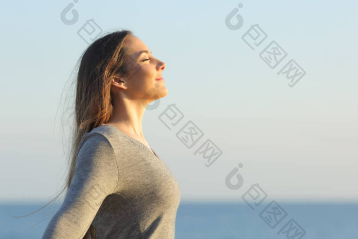 一位在海滩上呼吸新鲜空气的悠闲女子的侧景图片-包图网企业站