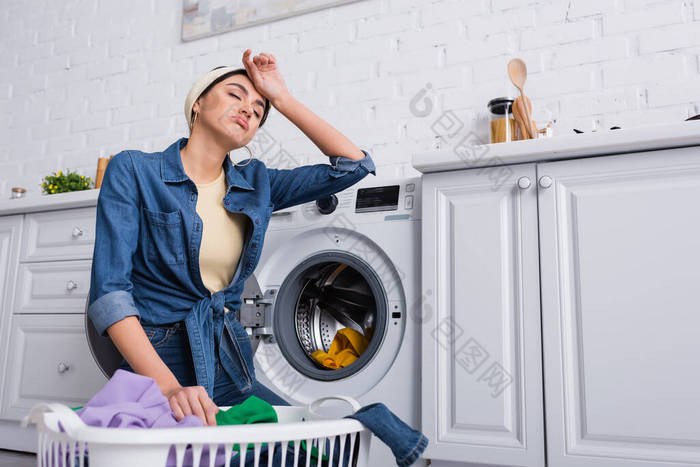 累坏了的家庭主妇带着衣服和洗衣机站在厨房图片-包图网企业站