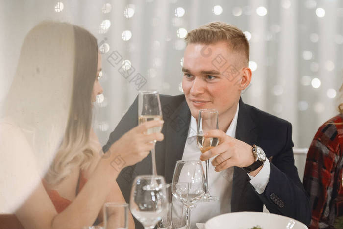 一对年轻夫妇坐在节日桌上喝着香槟酒面带微 包图企业站
