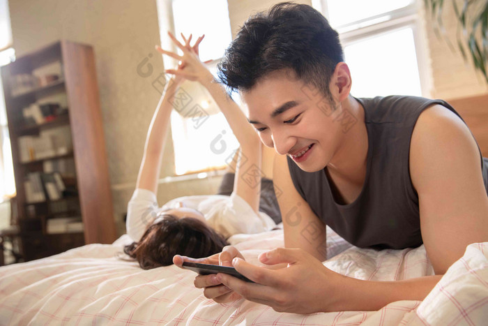 青年情侣趴在床上玩手机图片 包图网企业站