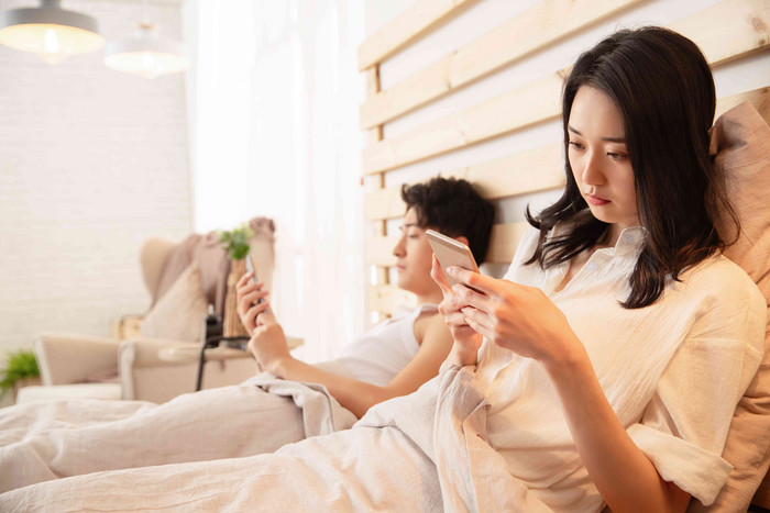 年轻情侣在床上使用手机 包图企业站
